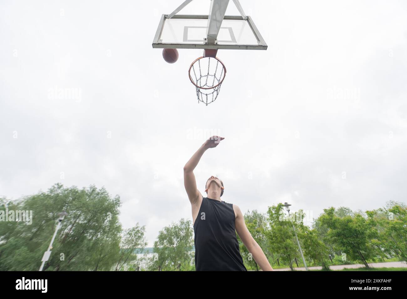 A Caucasian man shoots a ball into a basketball basket outdoors Stock ...