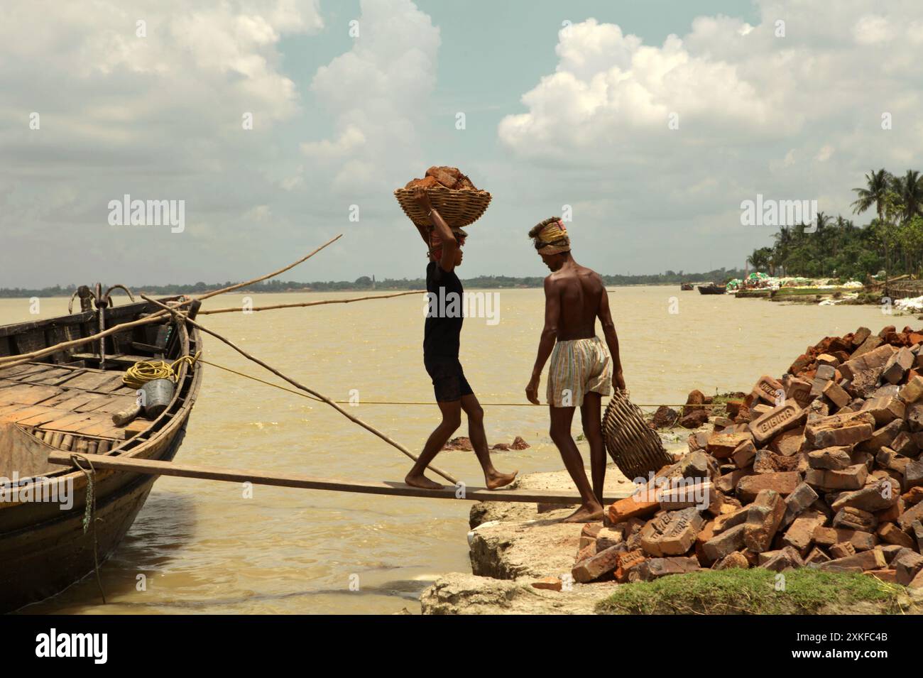 A worker walks on a woodboard connecting a boat and riverbank, as he is ...