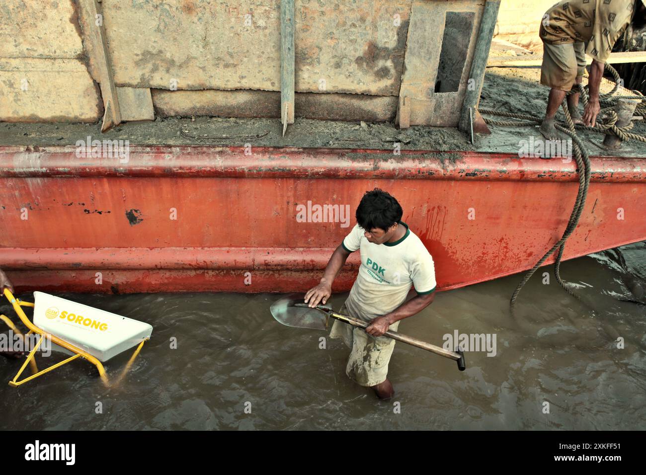 A worker cleans his shovel after unloading sand from a barge, as he is ...
