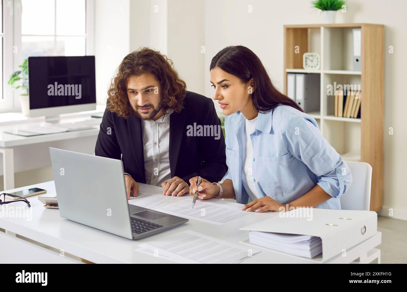 Two company employees sitting with laptop computer in office looking at ...
