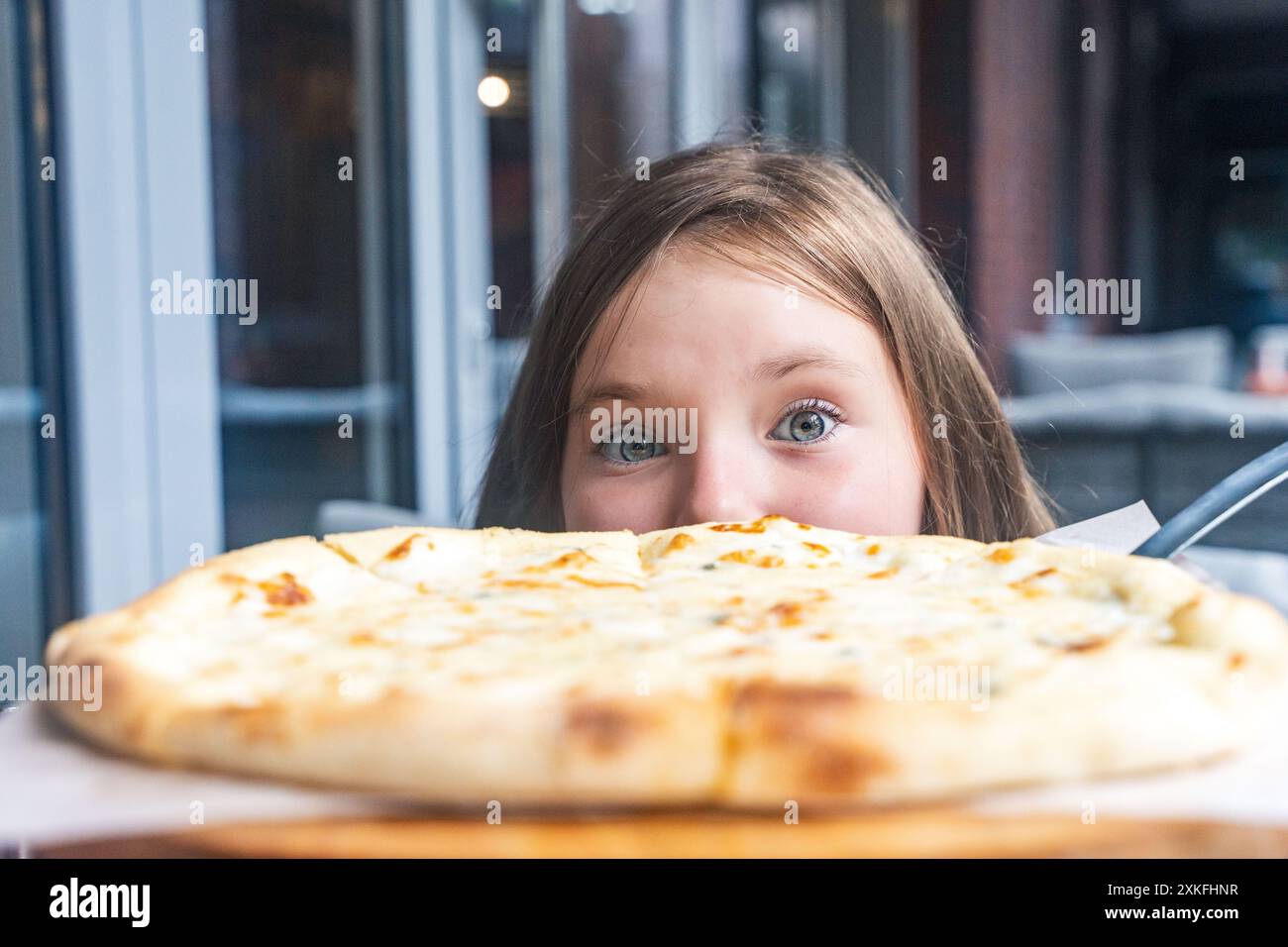 Cute girl and four cheese pizza close-up. A pre-teen girl looks into ...