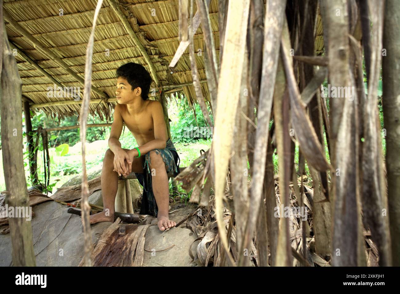 A tourism worker wearing indigenous attire sits on a hut, where tree ...