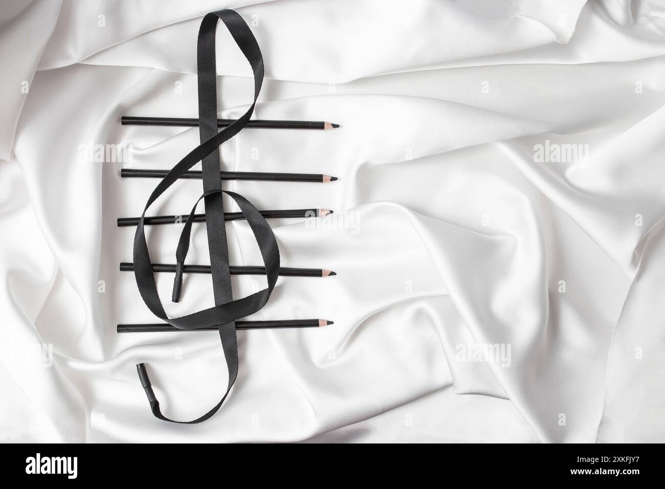 Treble clef made with black ribbon on five black crayons lines on white ...