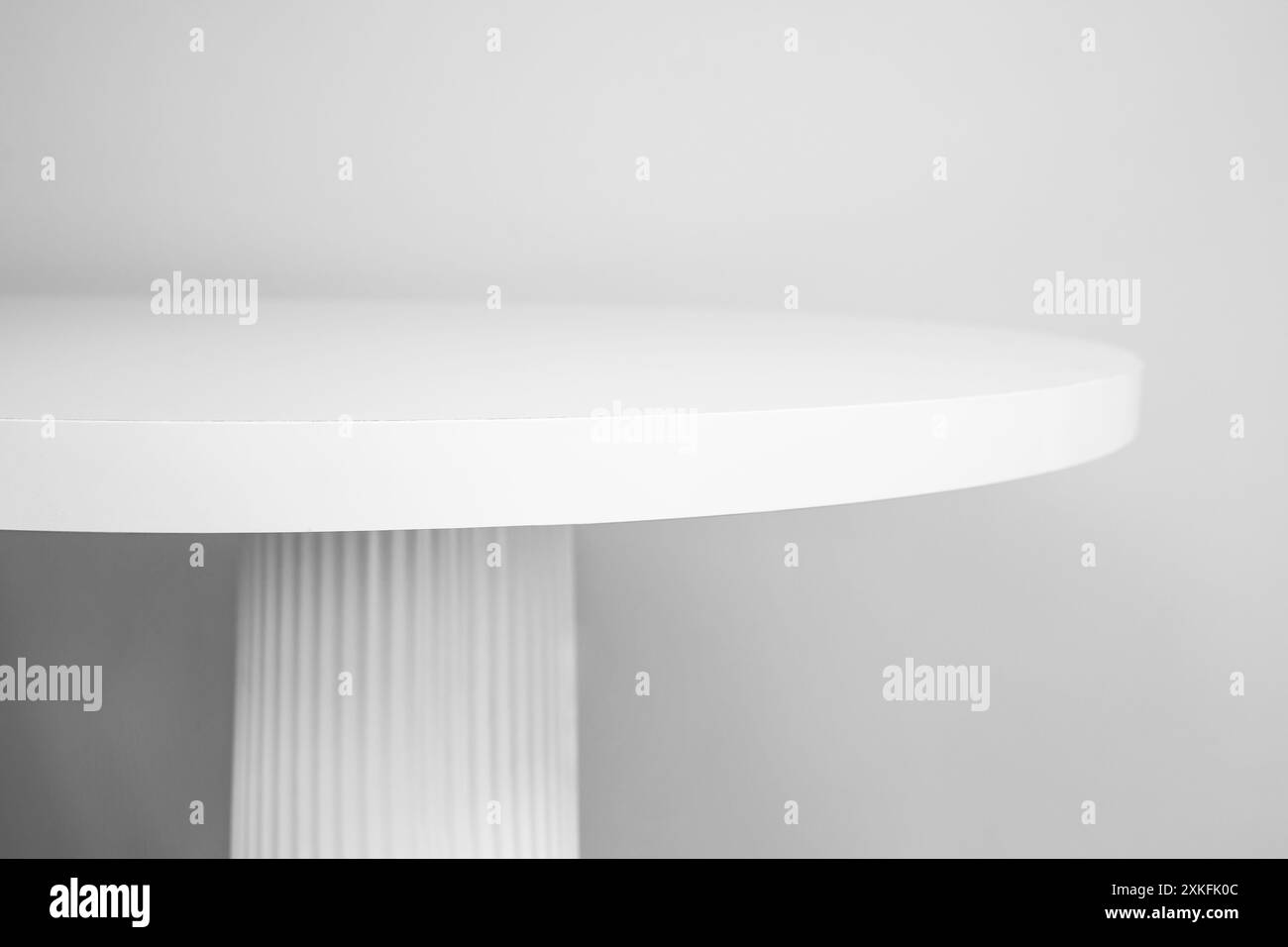 White round table top with column leg, side view on gray wall ...