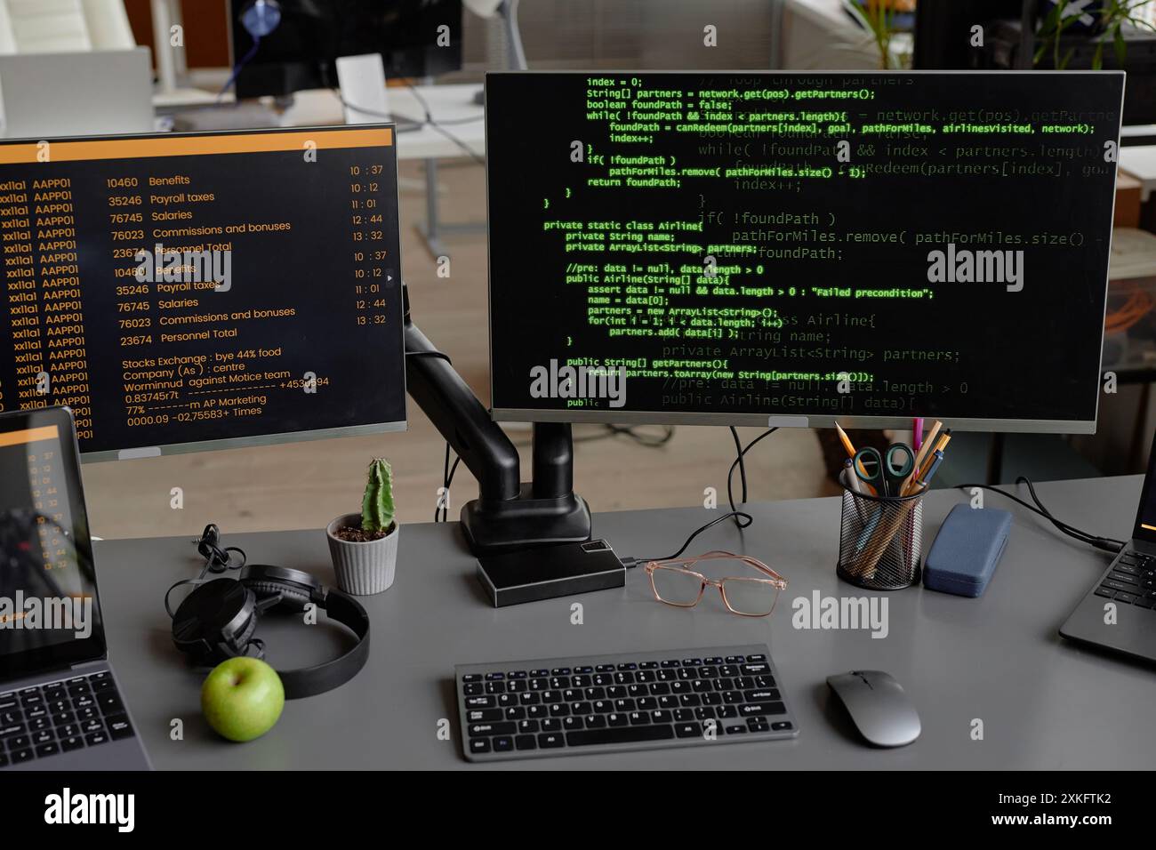 Still life shot of programmer work desk with headphones and multiple computers showing lines of ...