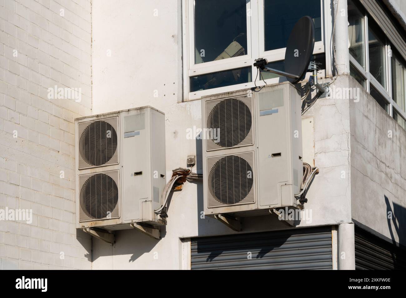 Two white air conditioners are mounted on the outside wall of a ...