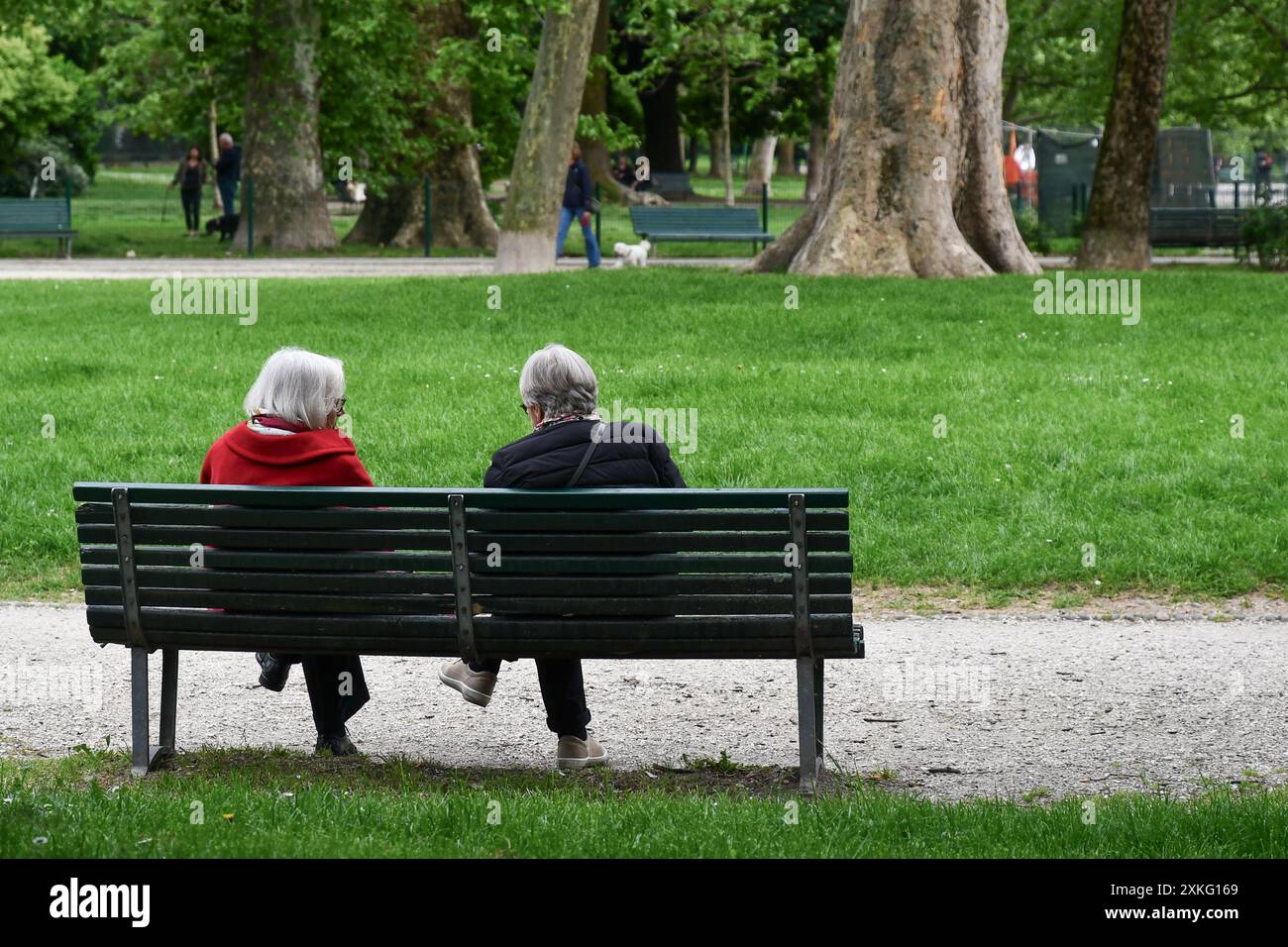 Rear view of two old ladies chatting on a bench in the Sempione Park, a ...