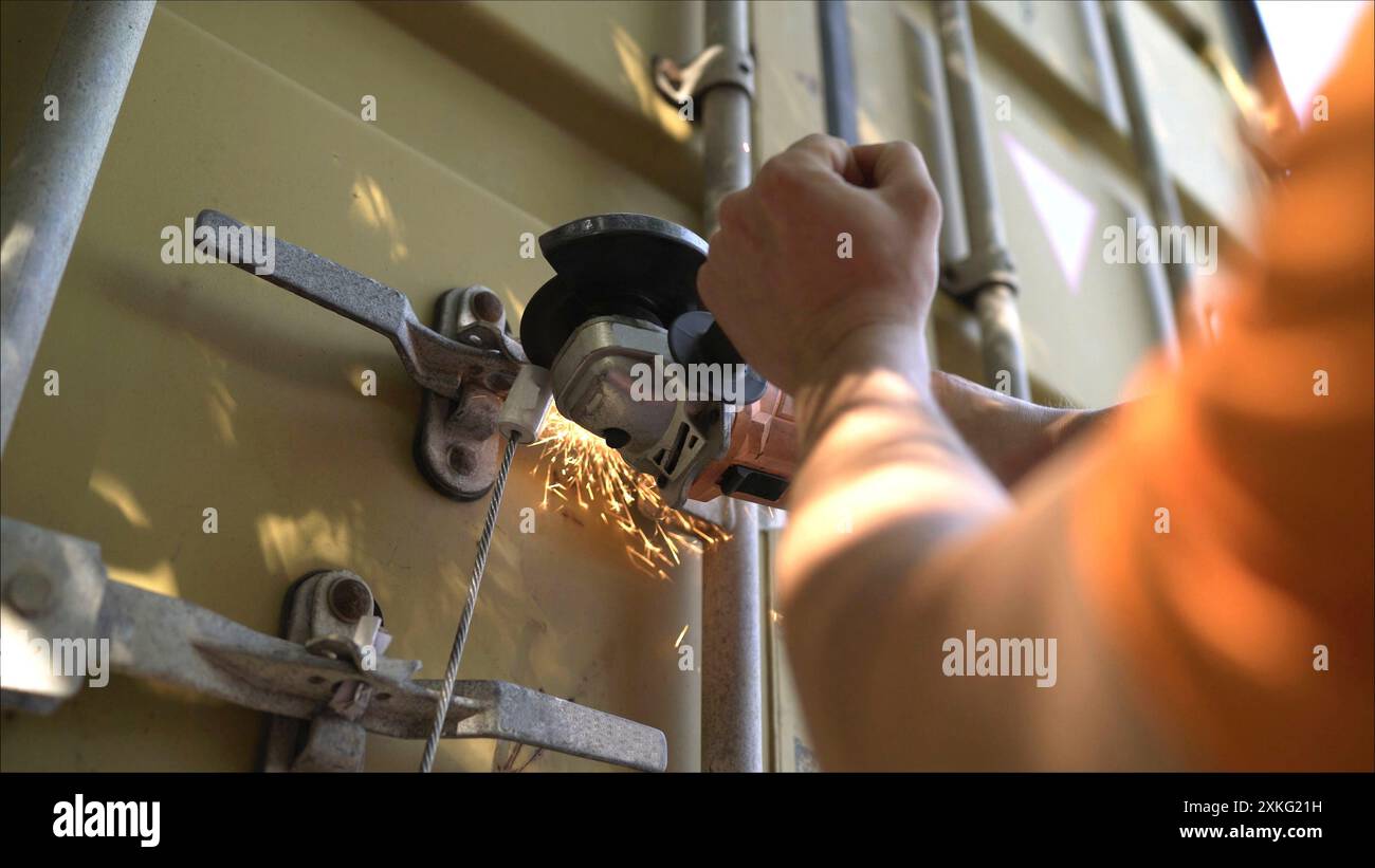 Close-up of a hand with a tool opening the lock of a large container ...