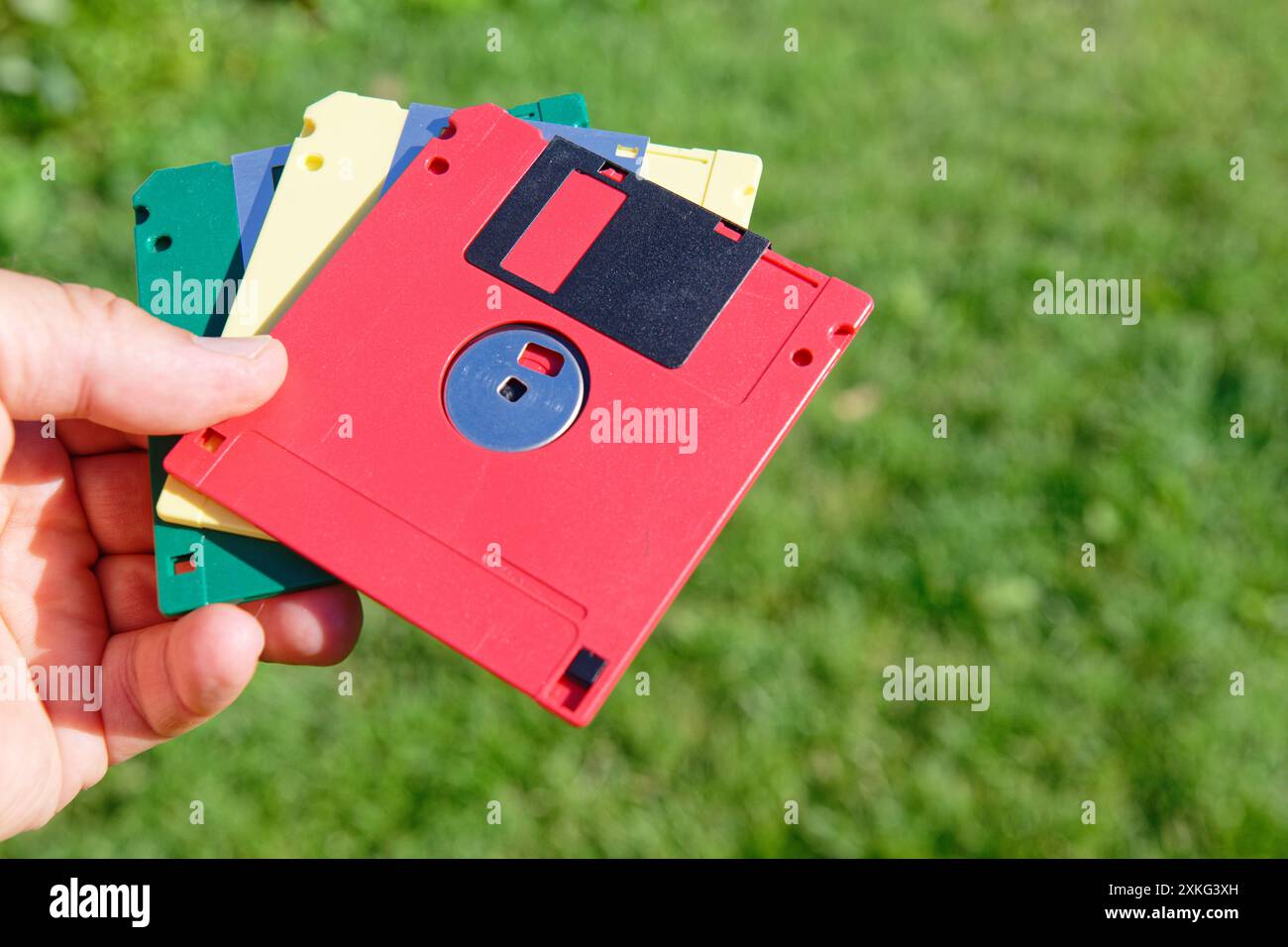 Vintage colored floppy disks in a hand on green grass lawn background ...