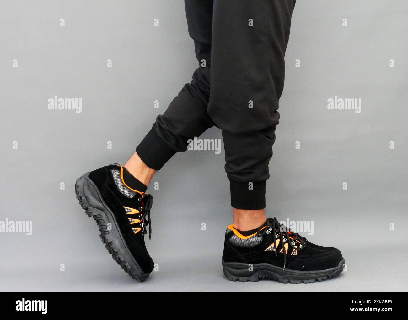 A male model wears black suede shoes with orange accents, featuring a ...