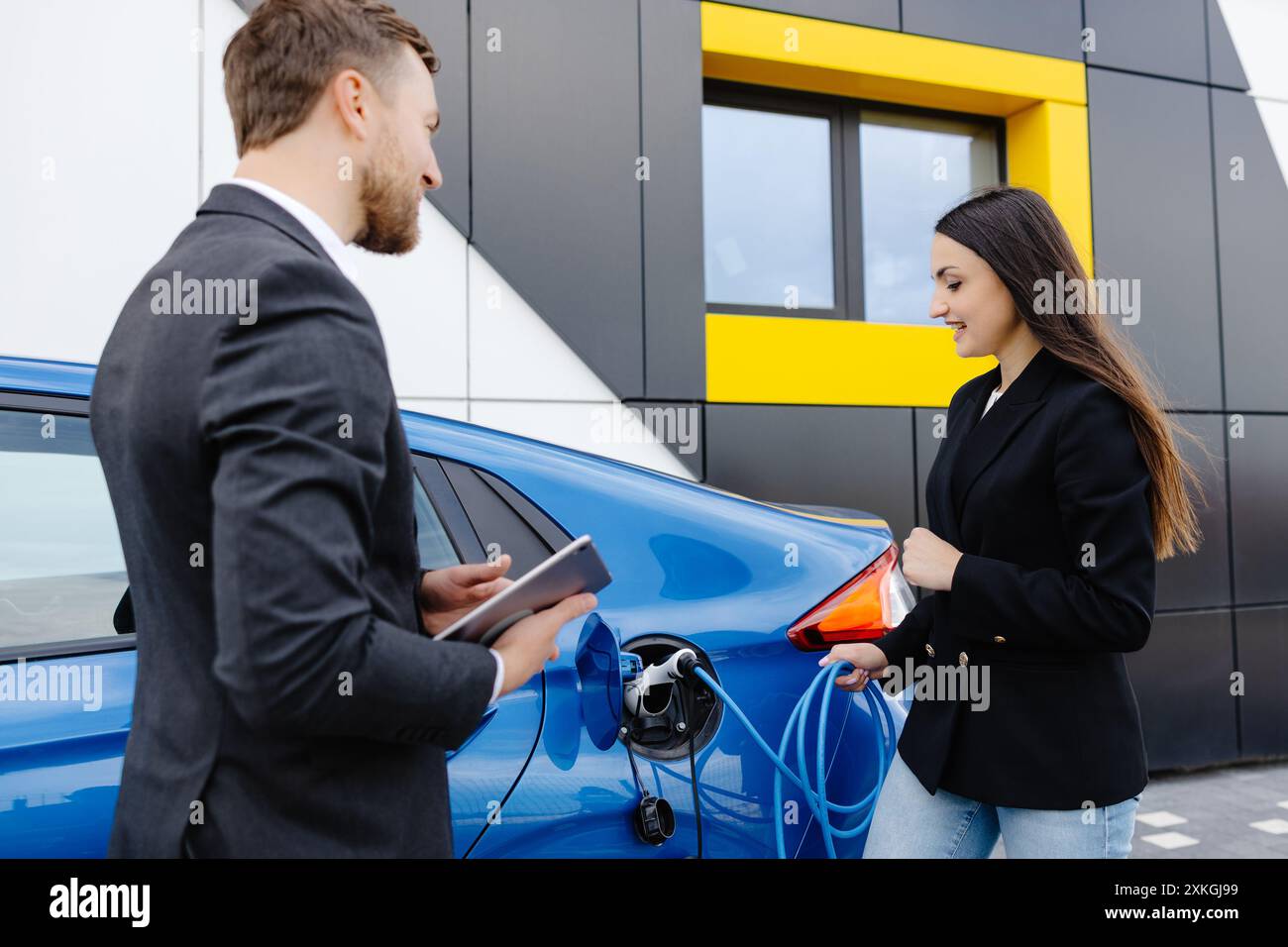 Sales manager showing how to charge electric car to a young client ...
