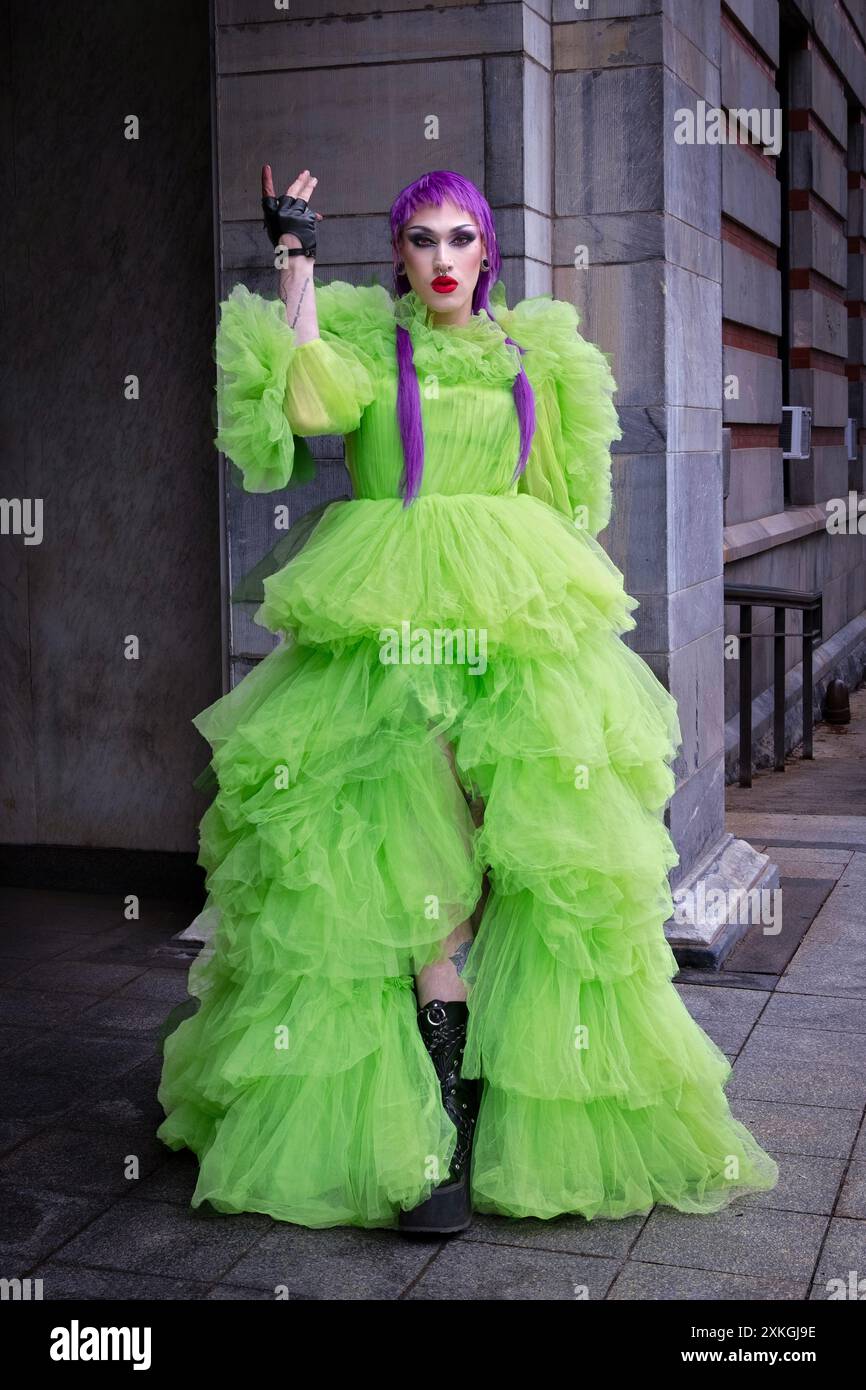A slender tall man in drag wearing an ornate green dress & purple hair ...