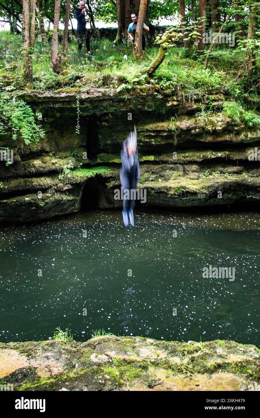 A woman jumping into a river from rocky, moss covered, cliffs. Hawes ...