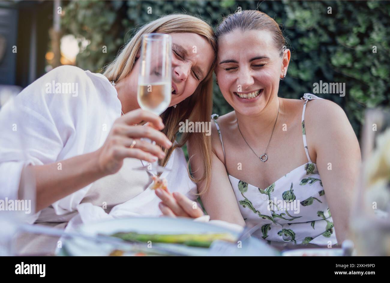 Two young women in dresses are laughing at joke and drinking champagne ...