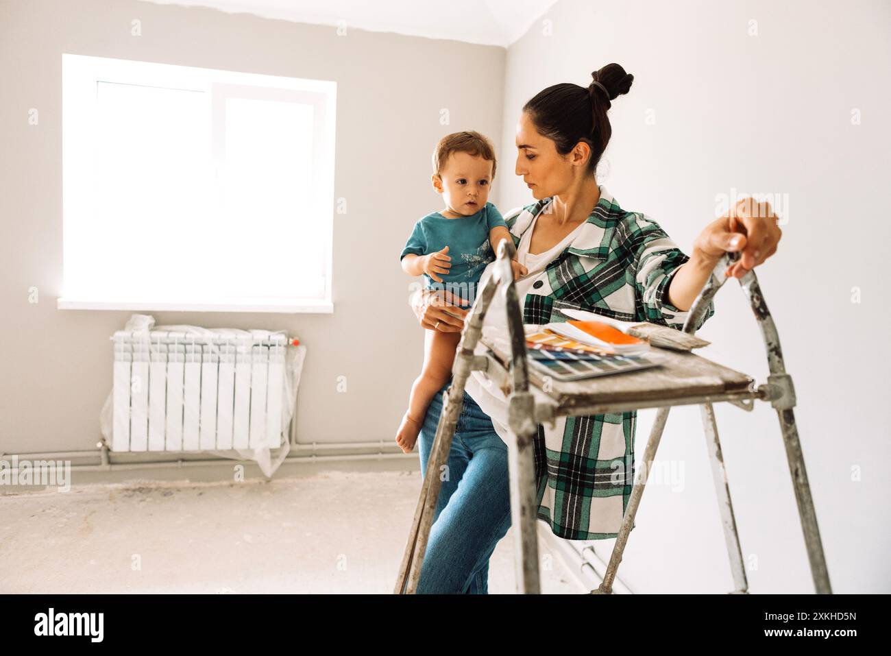 Young woman with child on ladder in renovated room. Attractive mother ...