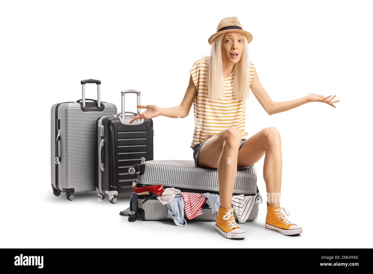 Confused young woman sitting on top of an overpacked suitcase isolated ...