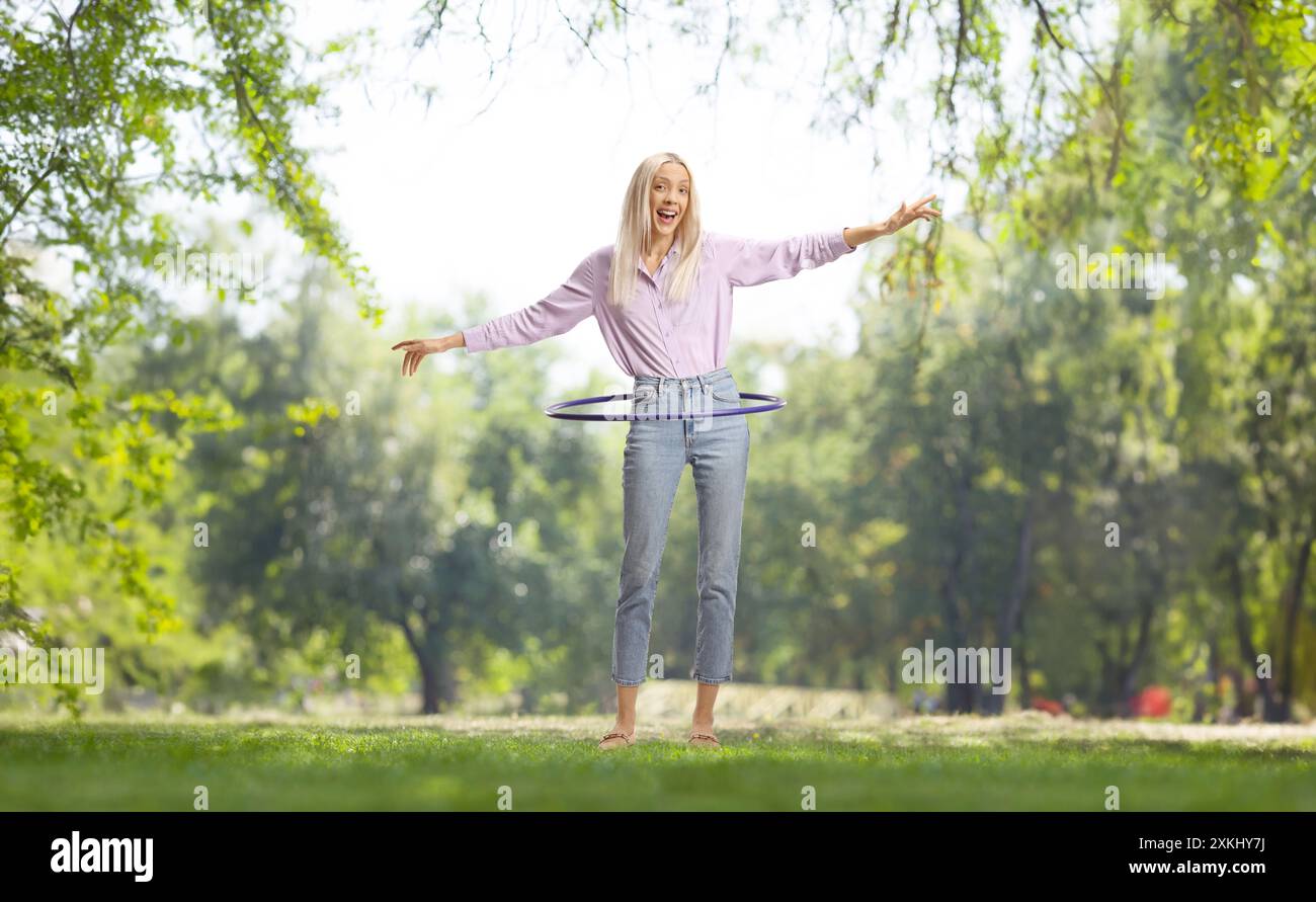 Full length shot of a happy young woman spinning a hula hoop in a park ...