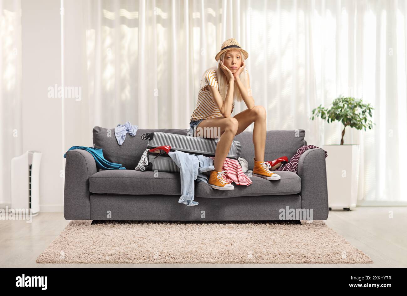 Sad woman with packed suitcase and clothes on a sofa Stock Photo - Alamy