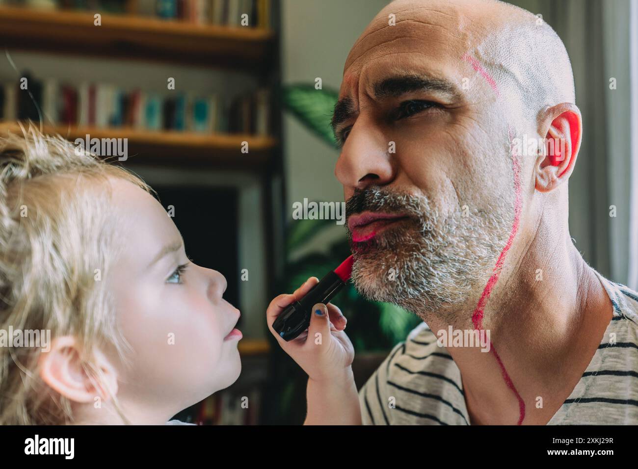 Little girl having fun putting lipstick on her father's face, who is ...