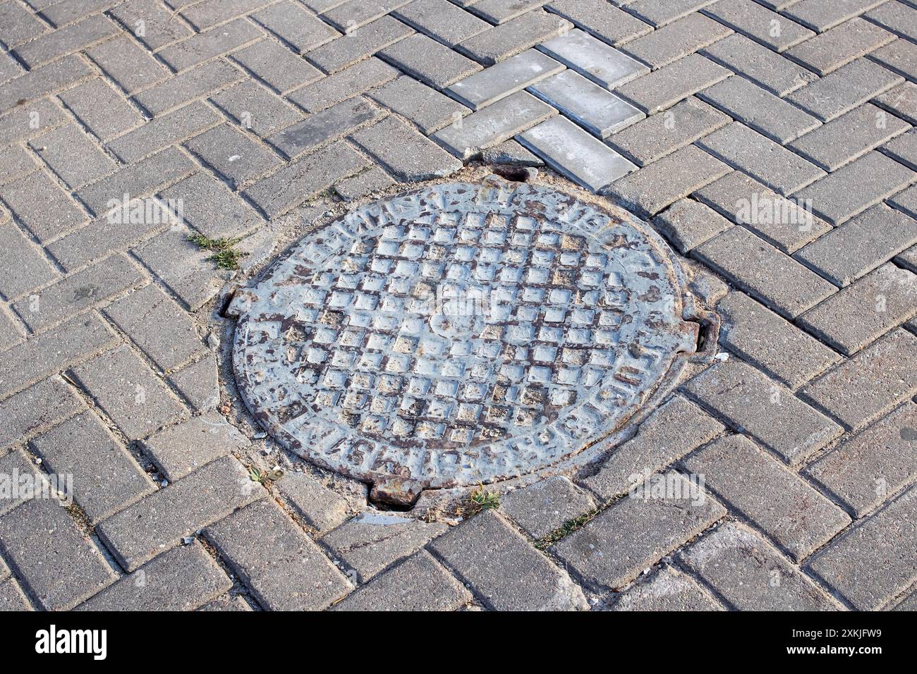 A round manhole cover lies atop a brick sidewalk, blending two ...