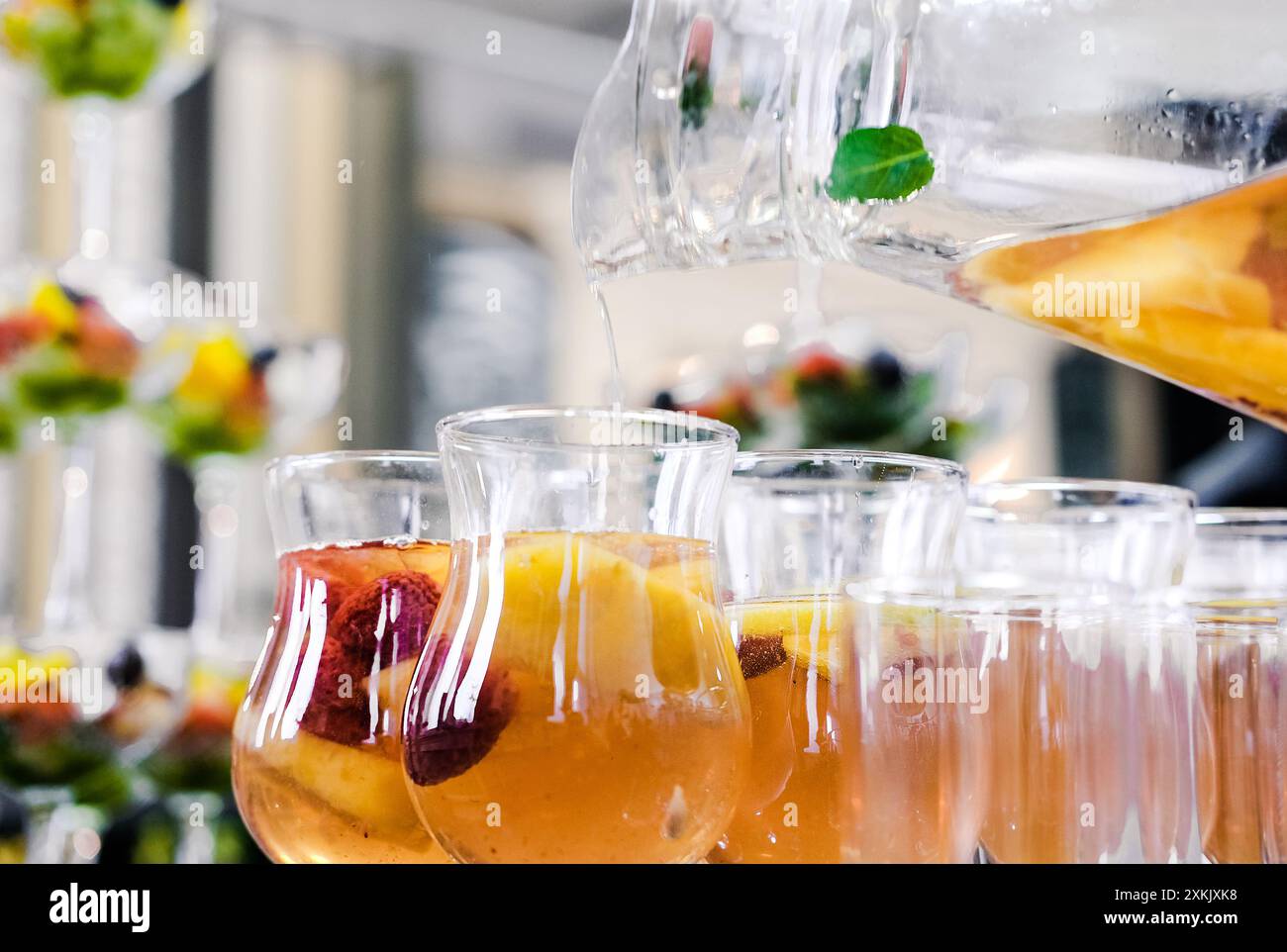 Bartender in black gloves and apron pouring fruit punch into glasses at an upscale event ...