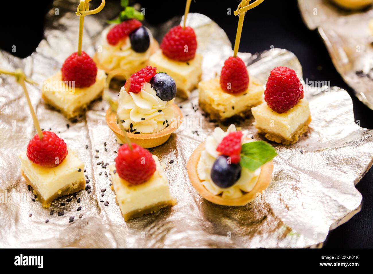 Assorted mini desserts with raspberries and blueberries on golden leaf ...