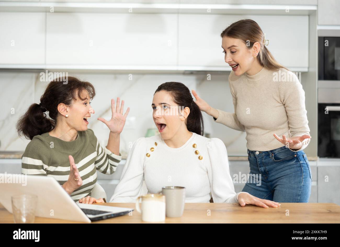 Three happy middle-aged woman expressing joy for winning in the kitchen ...
