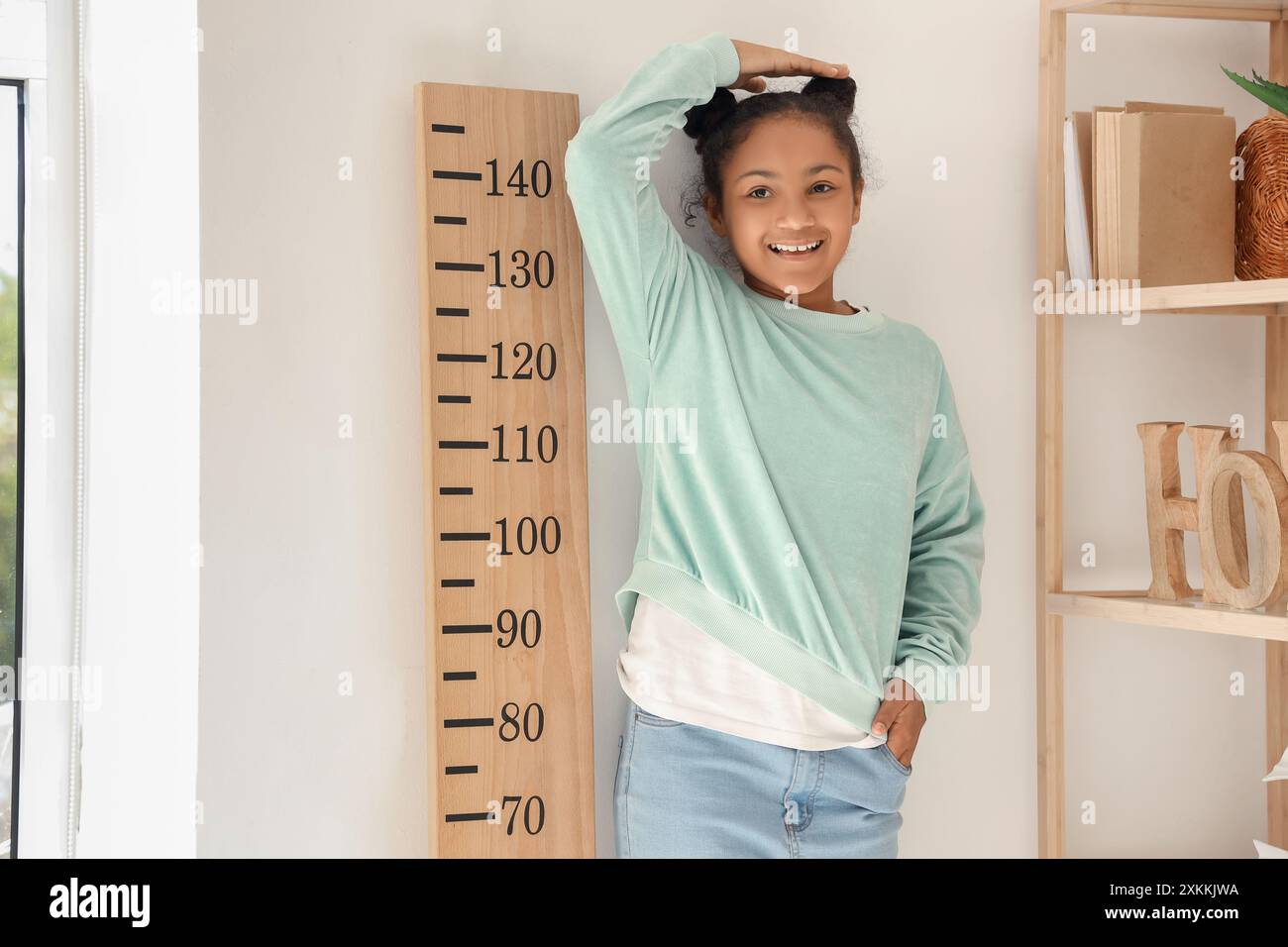 Little African-American girl measuring height near stadiometer at home ...