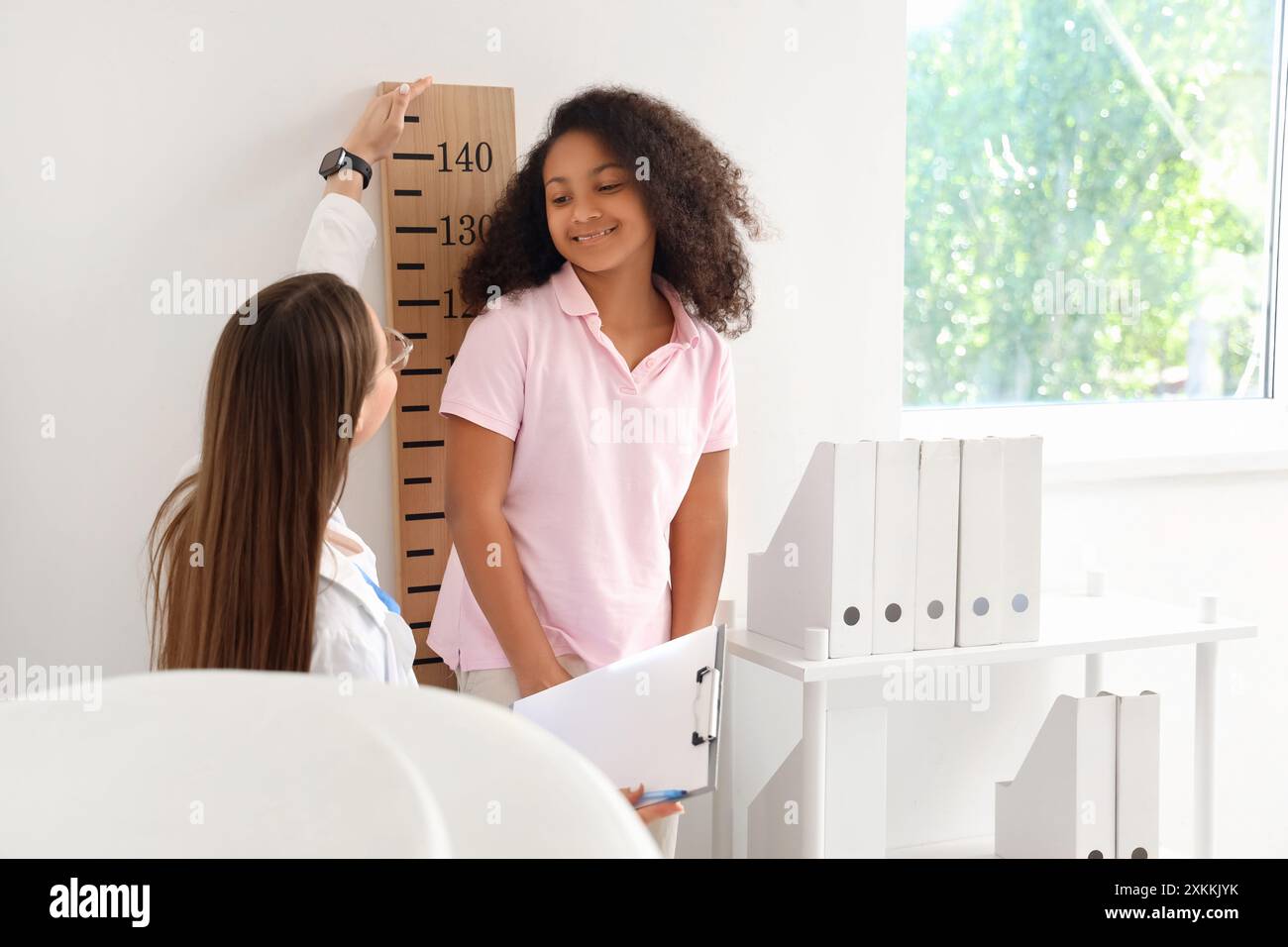 Female pediatrician with little African-American girl measuring height ...