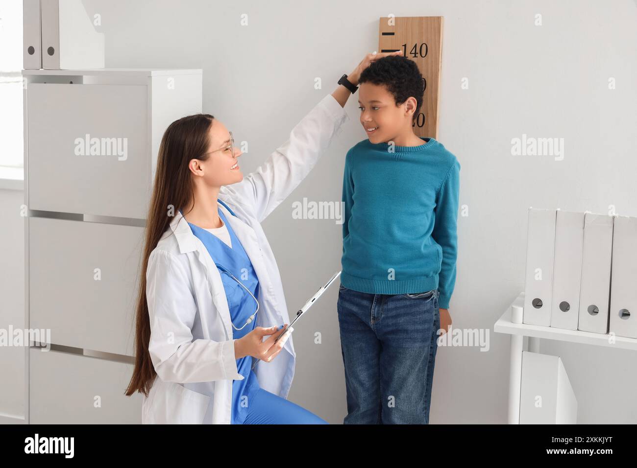 Female pediatrician with little African-American boy measuring height ...