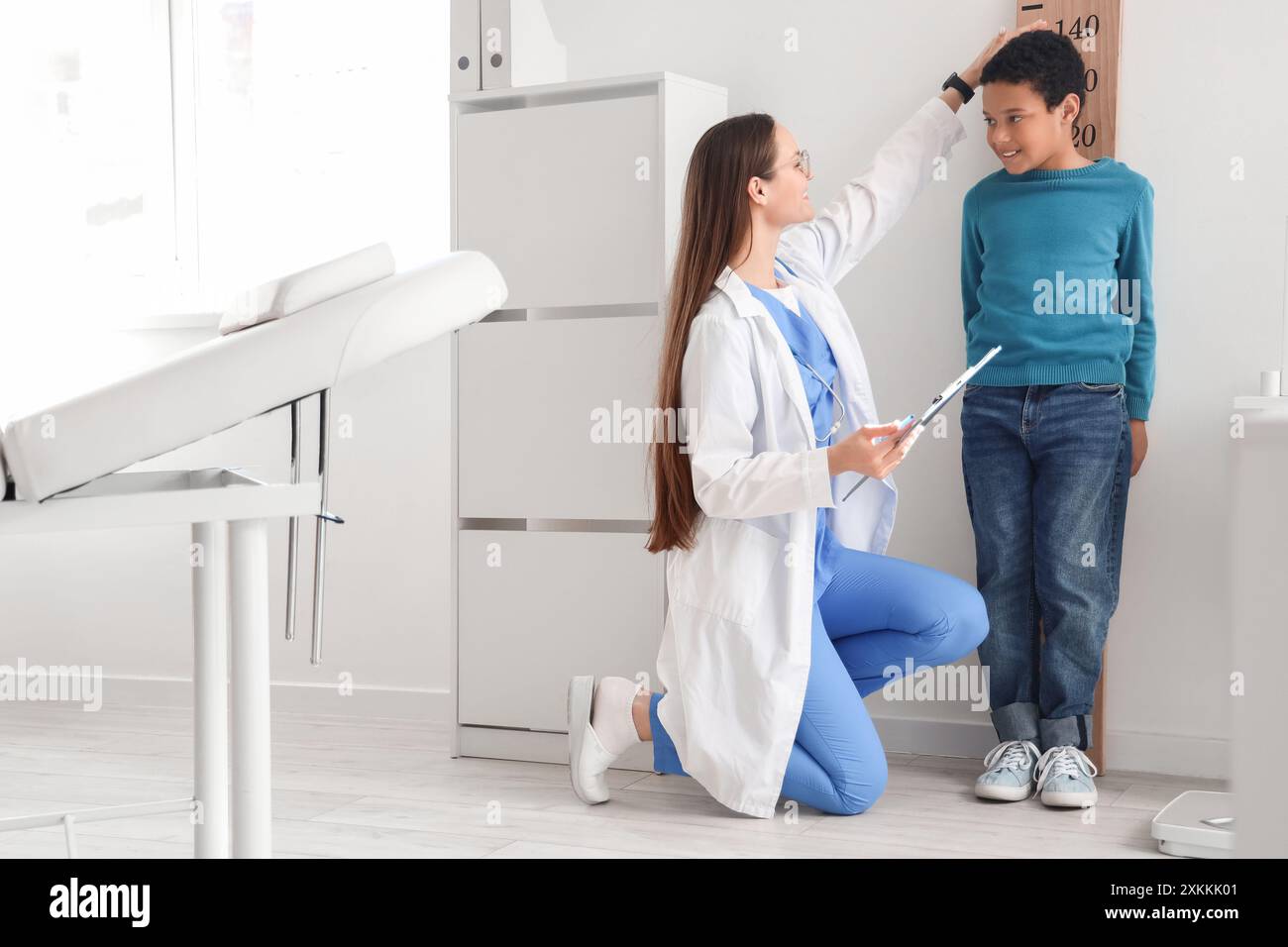 Female pediatrician with little African-American boy measuring height ...