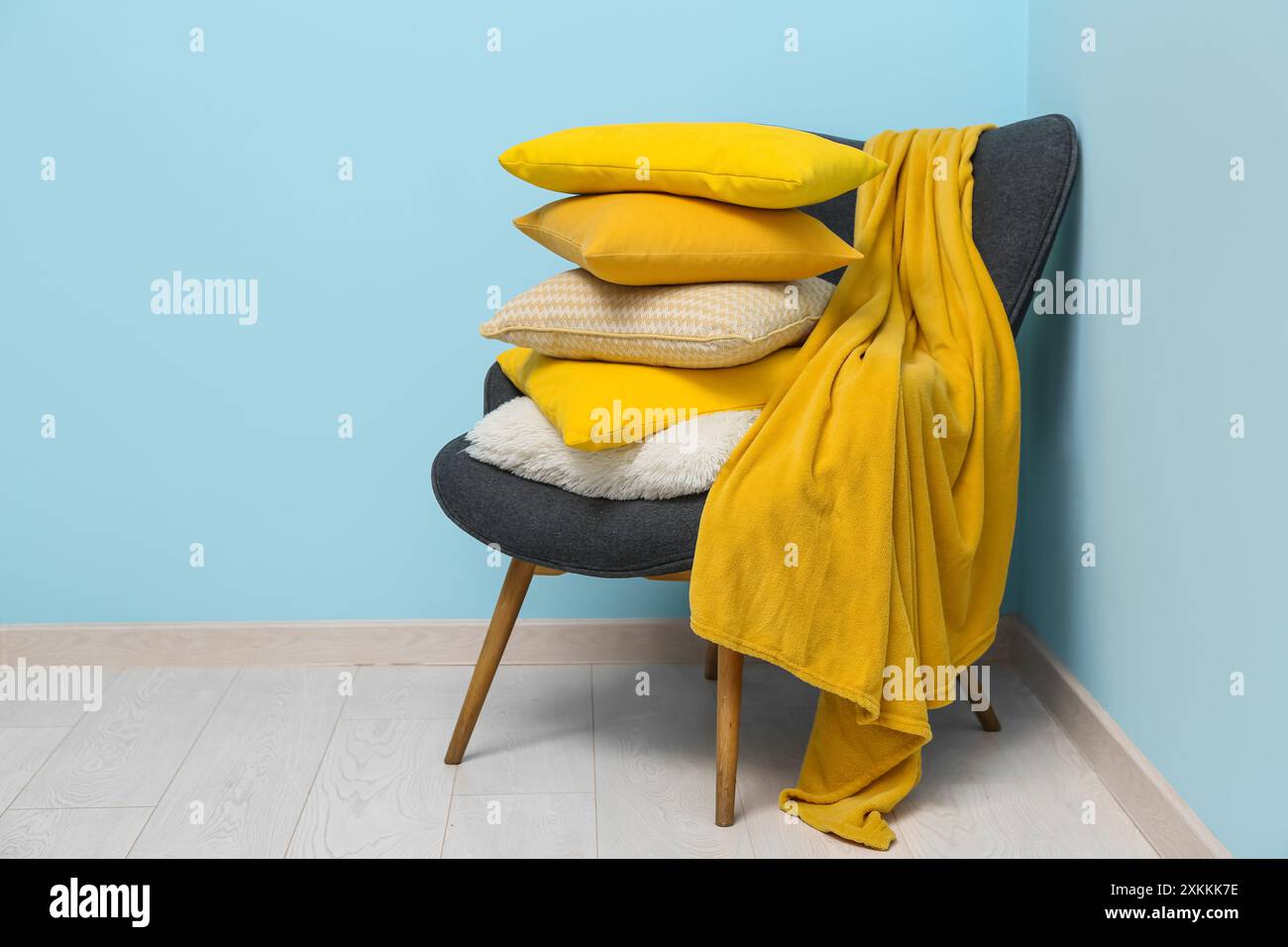 Stack of cushions and plaid on armchair near blue wall in room Stock ...