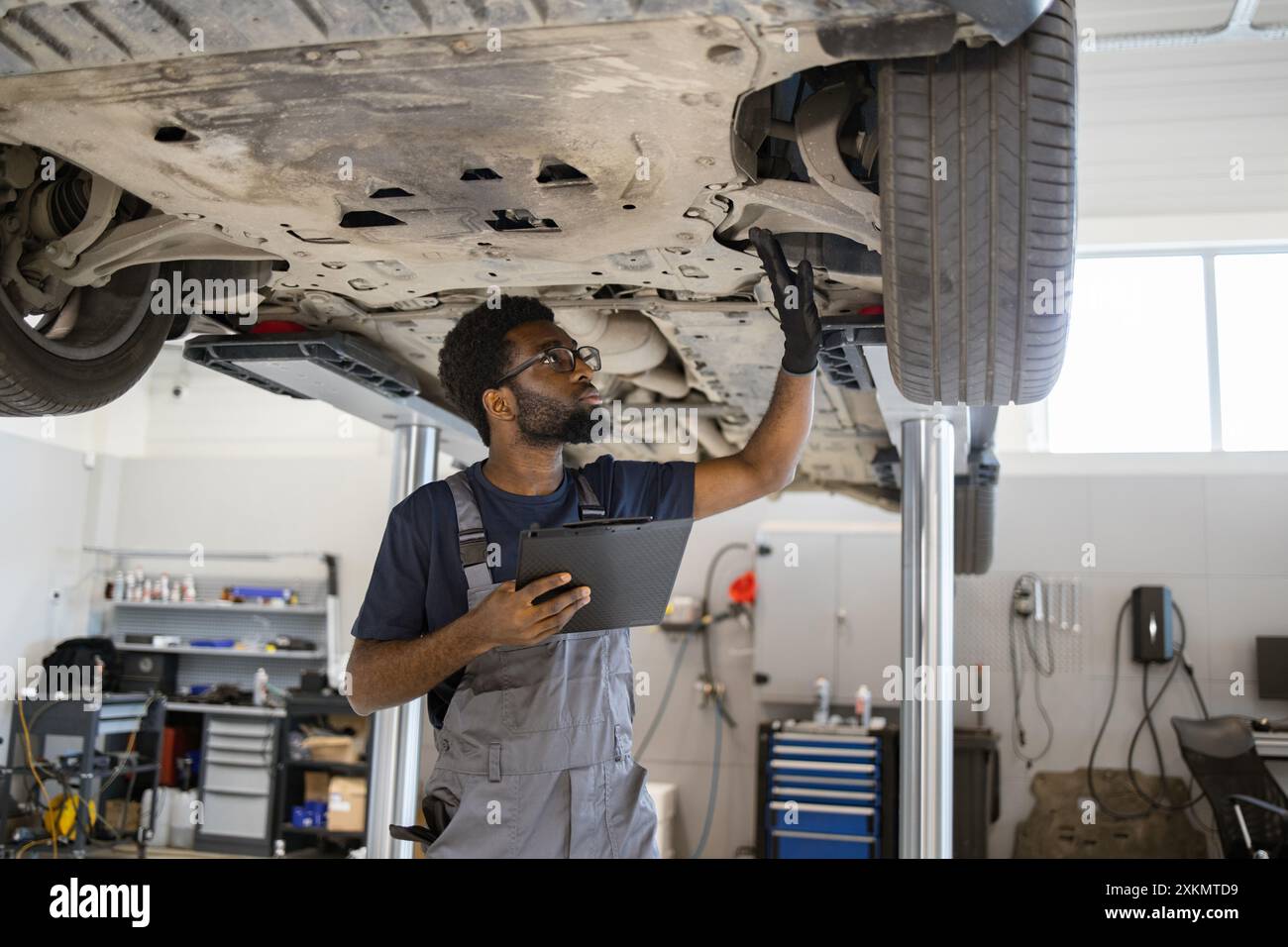 Mechanic inspecting car on lift in modern auto repair shop Stock Photo ...