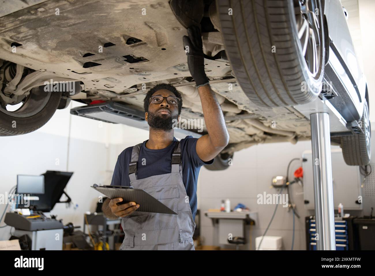 Mechanic inspecting car on lift in auto repair shop Stock Photo - Alamy