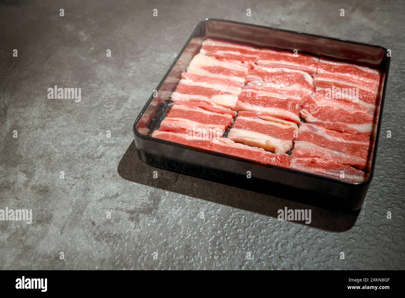 A tray of meat is on a grey surface. The meat is sliced and arranged in ...