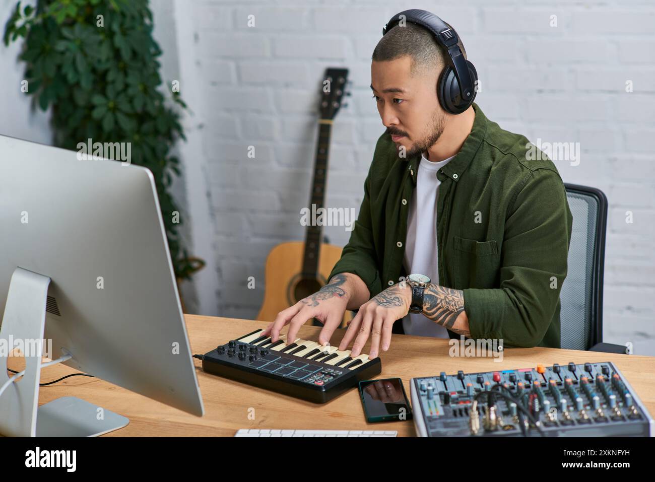 An Asian man plays a midi keyboard in his studio, surrounded by musical ...