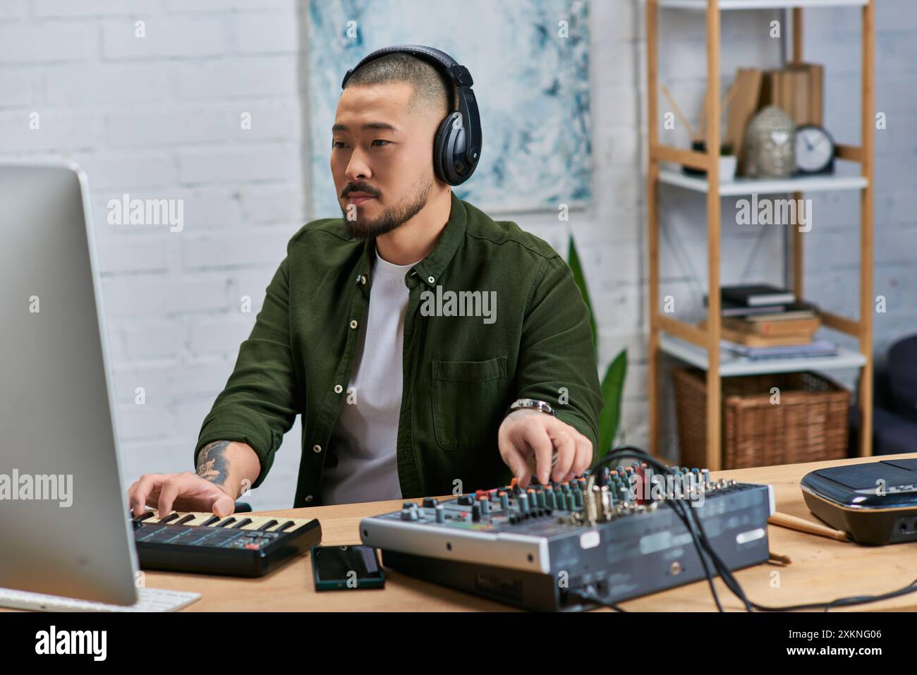 A handsome Asian man wearing headphones, works on music in his studio ...