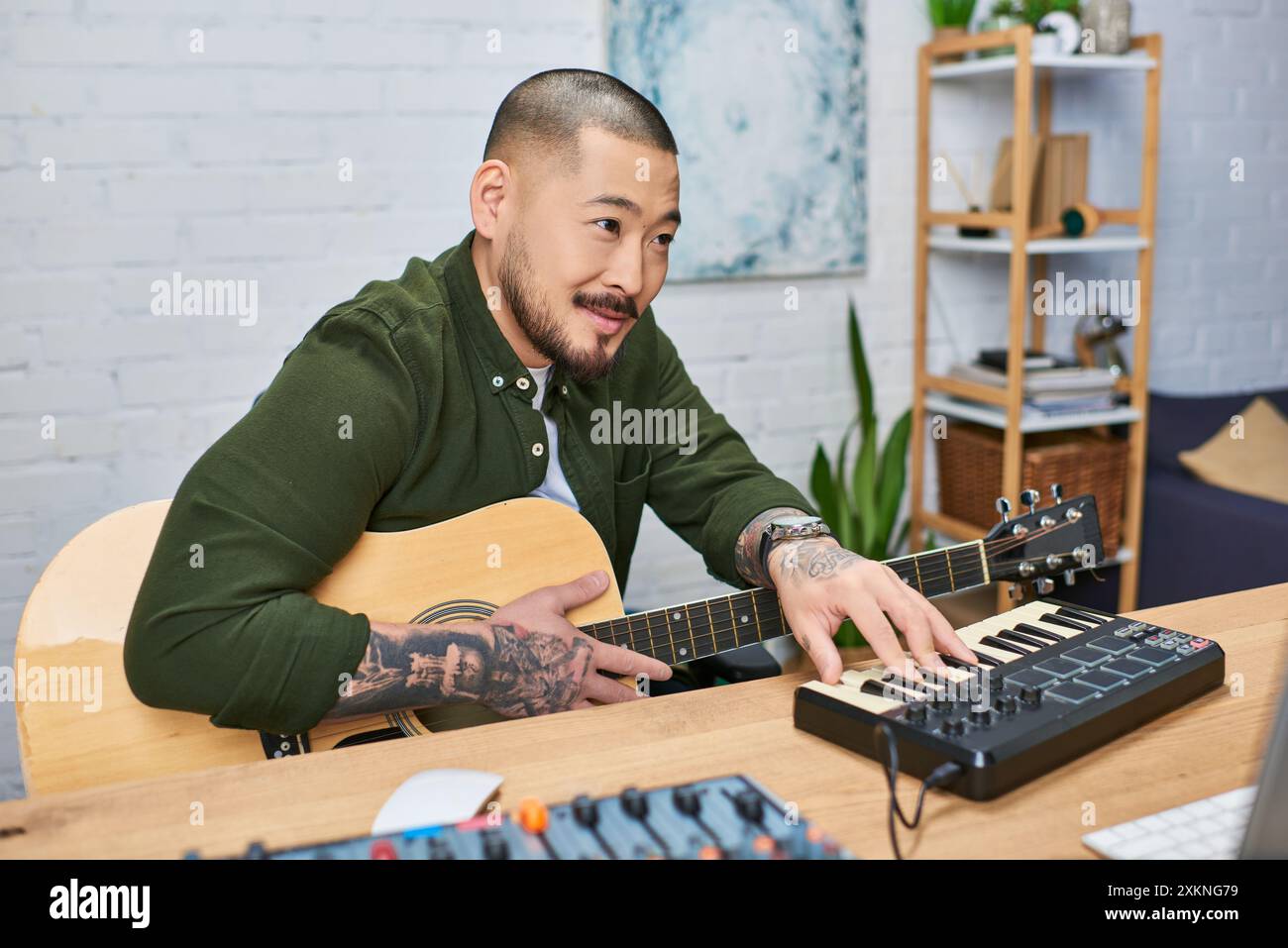 A handsome Asian man plays the guitar and MIDI keyboard while creating ...