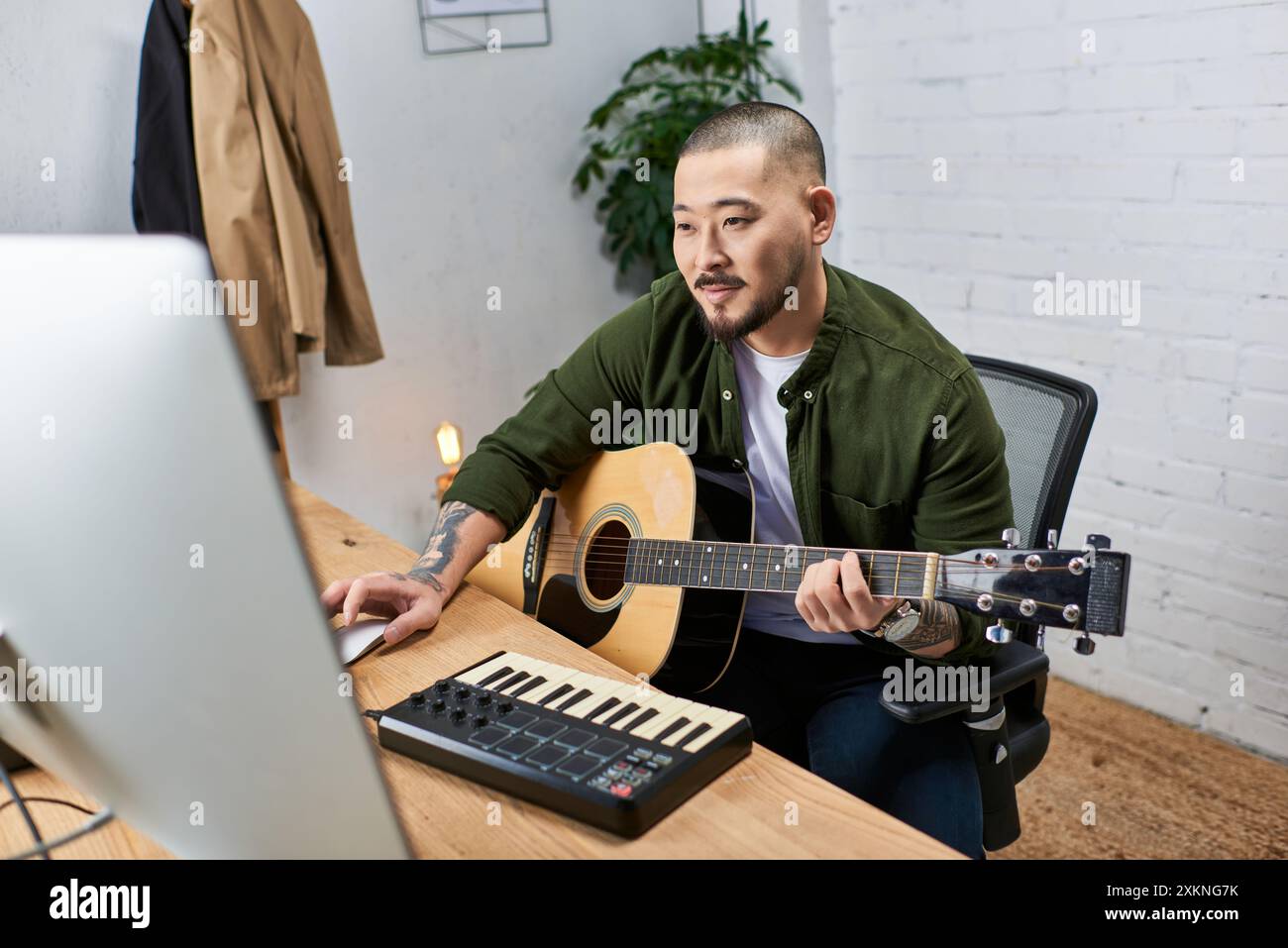 A young Asian man plays an acoustic guitar and uses a keyboard in his ...