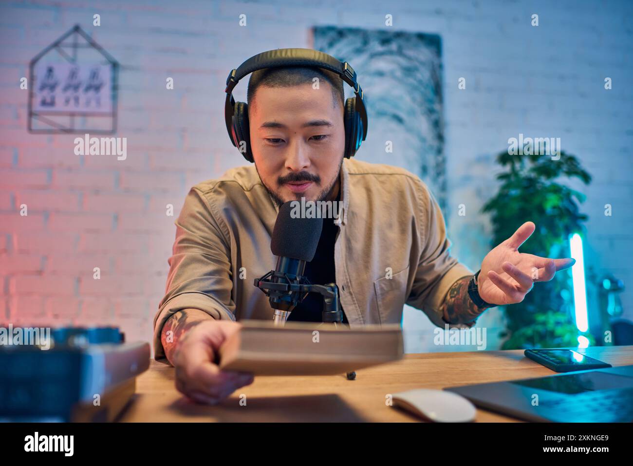A handsome Asian man records a podcast in his studio, holding a book ...