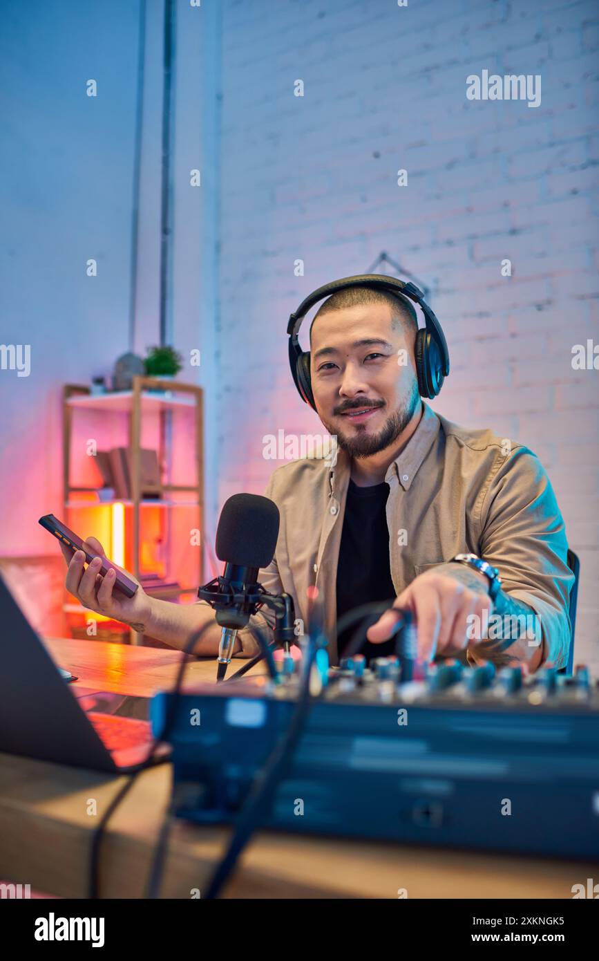 A handsome Asian man wearing headphones smiles while podcasting in his home studio Stock Photo ...