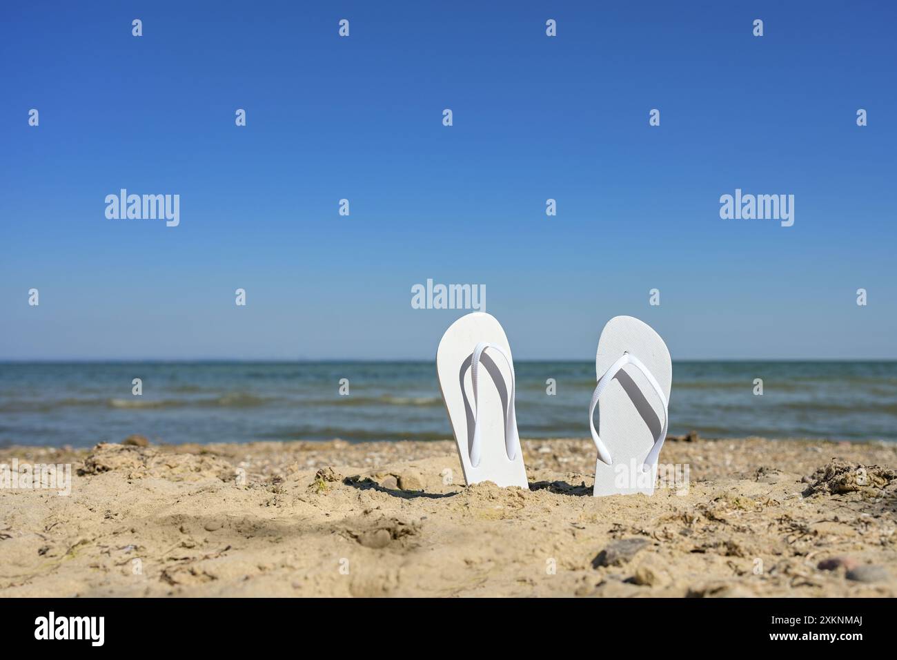 Pair of white flip flop sandals stuck in the beach by the sea against a ...