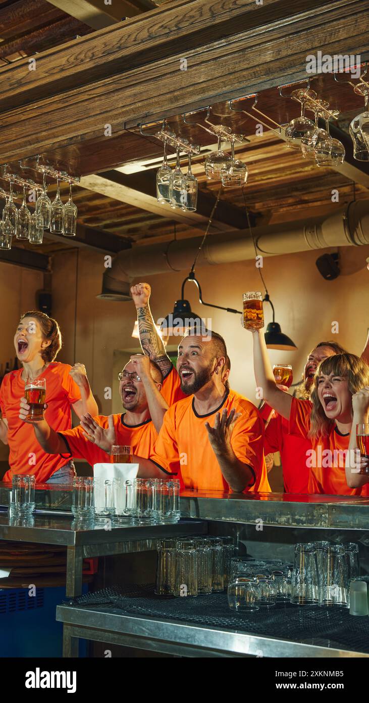 Friends in orange shirts cheer enthusiastically at bar, raising their ...