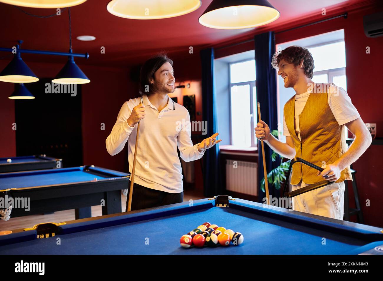 Friends stand by a pool table, laughing and talking, before a game of ...