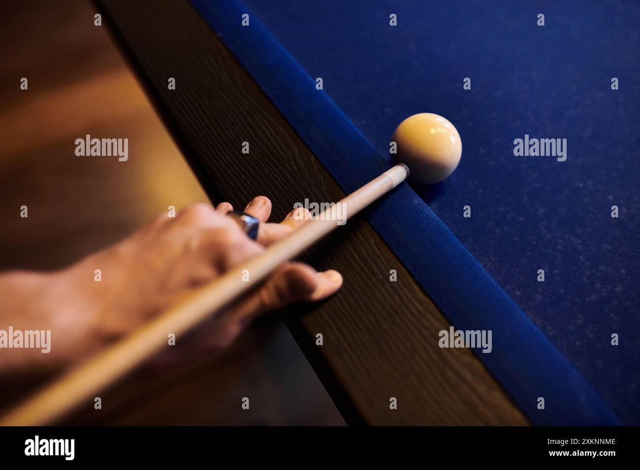 A close-up of a hand holding a pool cue, aimed at a white ball on the ...