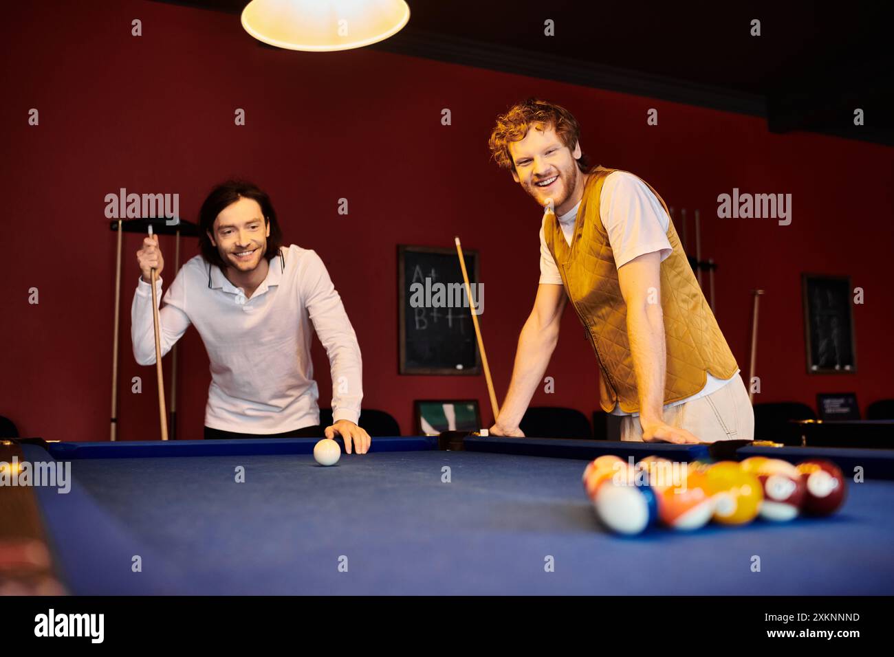 Two men in casual clothing play pool together in a dimly lit room Stock ...