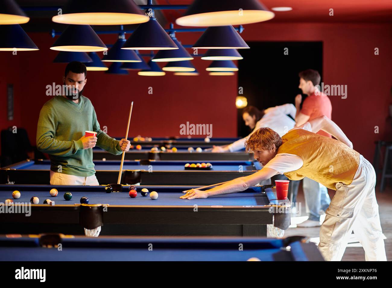 Friends enjoy a casual game of billiards in a dimly lit room with a red ...