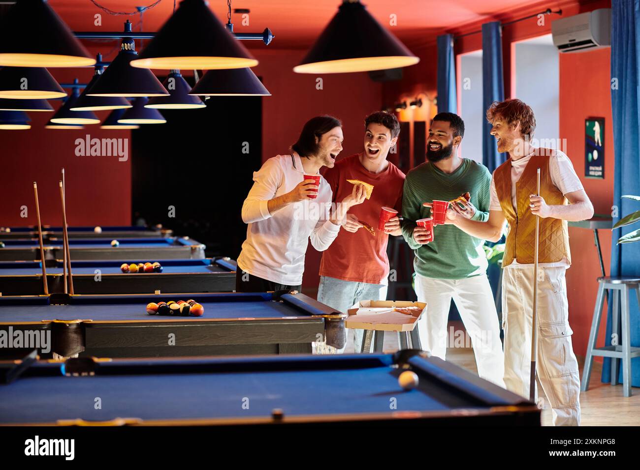 Friends stand around a pool table in a dimly lit billiards hall ...