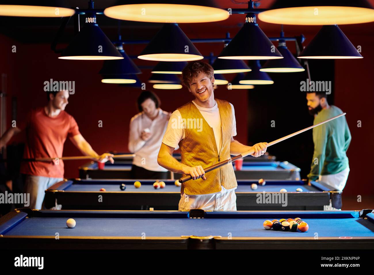 A group of friends play pool together in a dimly lit billiard hall ...