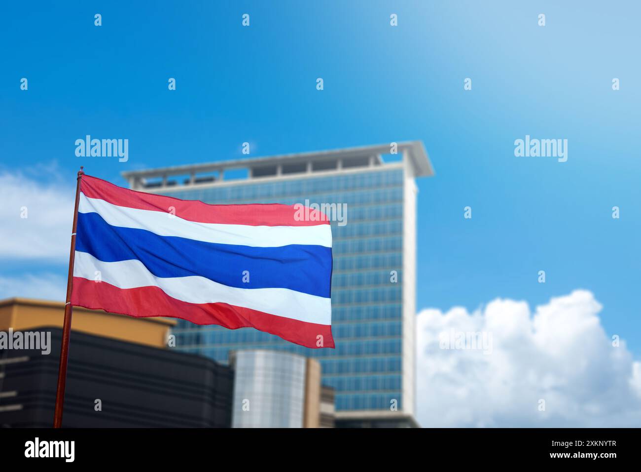 A Thailand flag with the colors red, white, and blue is flying in front ...